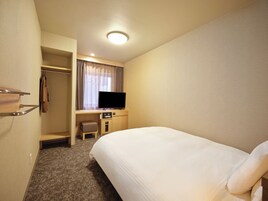 Quarto de hotel com cama, secretária, televisão, guarda-roupa e chão coberto de carpete.