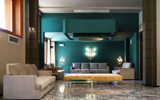 Um lobby moderno com paredes verde-água, piso de mármore e área de estar com sofás e poltronas.