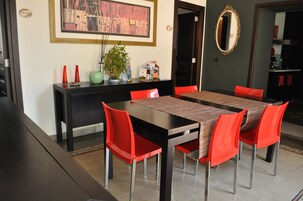 Uma sala de jantar com uma mesa preta, cadeiras vermelhas e um espelho decorativo na parede.