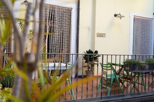 Uma varanda com grade de metal, cadeiras verdes, uma mesa e um vaso de planta.