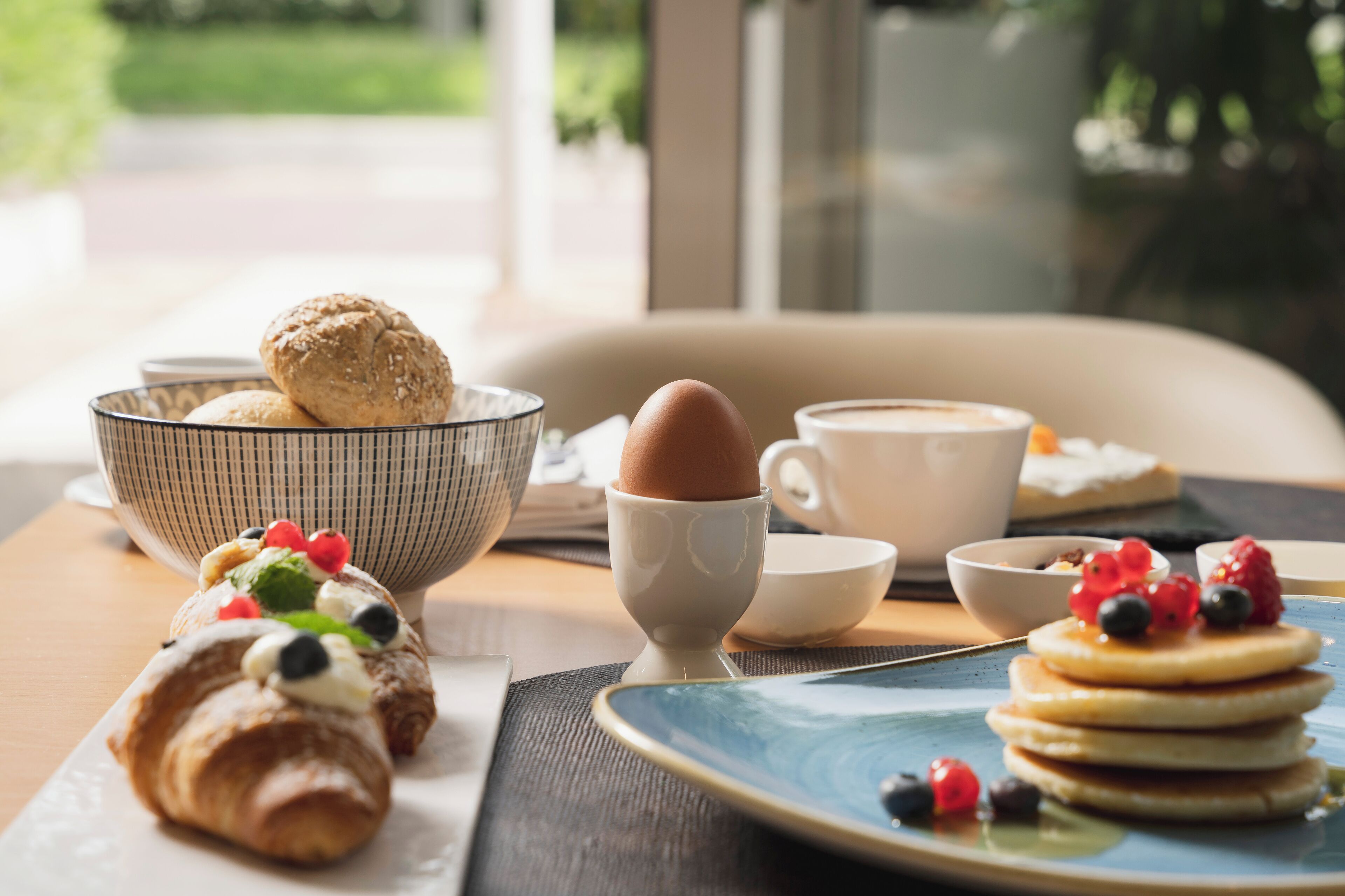 Uma mesa posta para o café da manhã, com croissants, panquecas e uma xícara de café.
