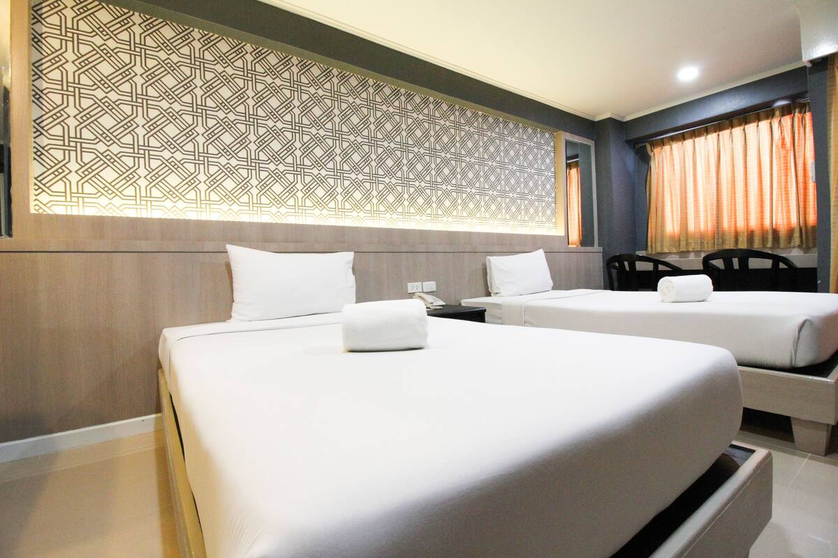 Quarto de hotel com duas camas, parede estampada e janela com cortinas.