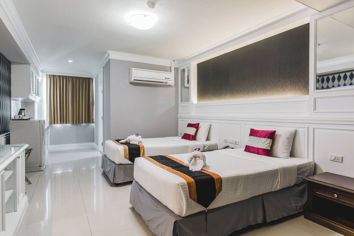Quarto de hotel com duas camas, uma escrivaninha, ar condicionado e um espelho grande.