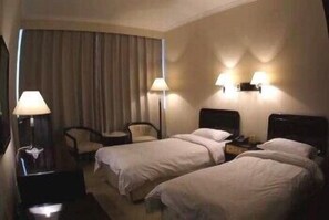 Quarto de hotel com duas camas, uma escrivaninha, uma cadeira e duas luminárias fixadas na parede.