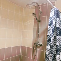 Um chuveiro com um chuveiro manual e um chuveiro de chuva fixado na parede, um cortina com padrão geométrico e paredes revestidas de azulejo em um banheiro.