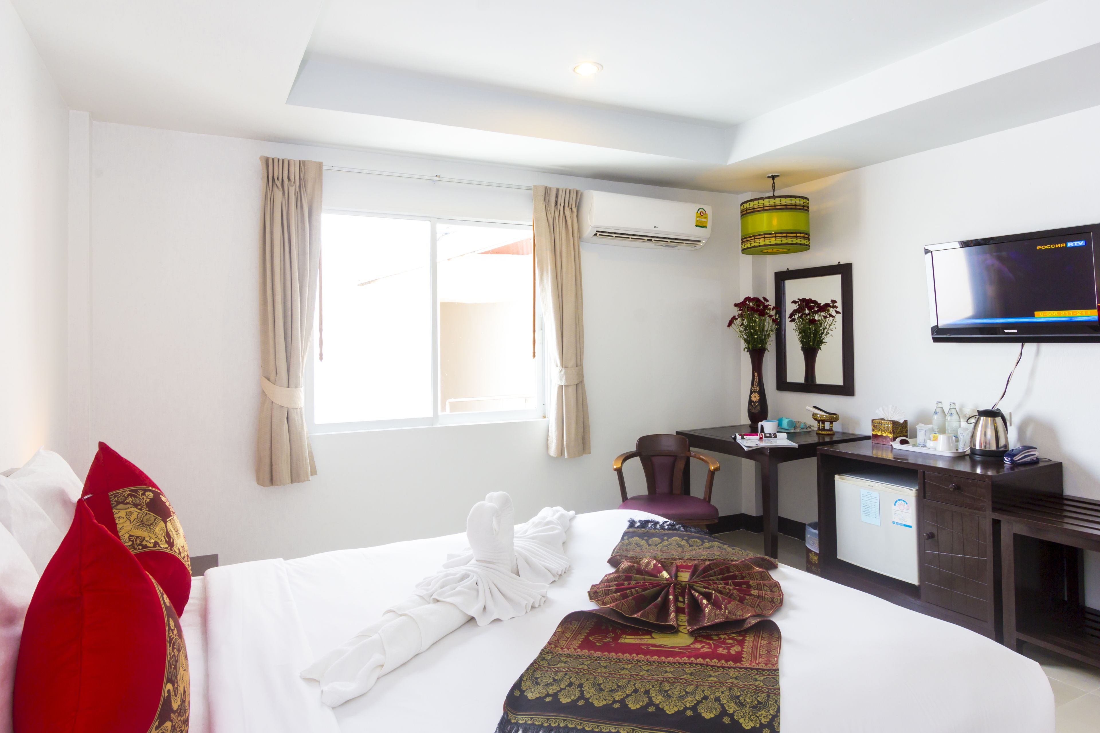Quarto de hotel com cama, escrivaninha, televisão e janela com cortinas.