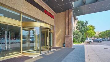 Entrada de hotel com porta giratória, fachada de vidro e vista para o estacionamento.