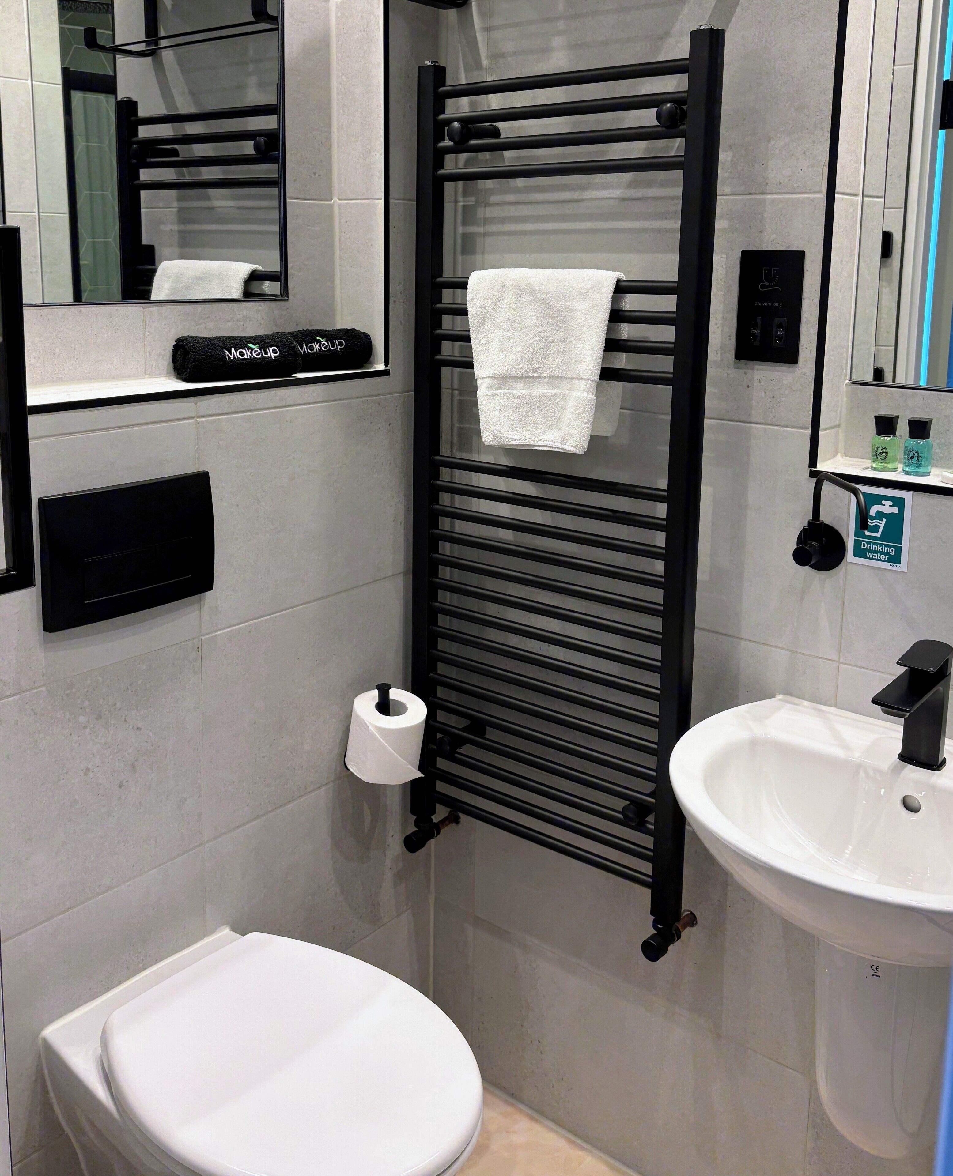 Um banheiro moderno com um porta-toalhas preto, vaso sanitário branco, pia e espelho.