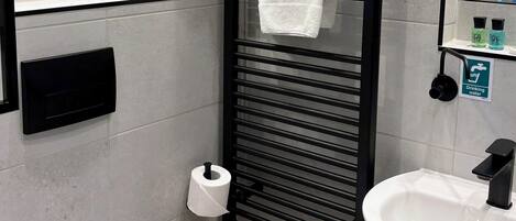 Um banheiro moderno com um porta-toalhas preto, vaso sanitário branco, pia e espelho.