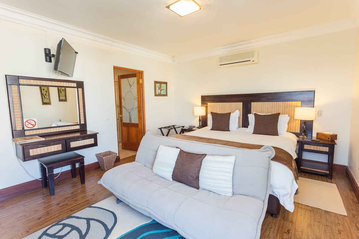 Quarto de hotel com uma cama grande, um sofá, uma escrivaninha e um espelho.