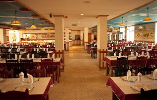 Um restaurante espaçoso com várias mesas e cadeiras, piso de azulejos e luminárias pendentes.
