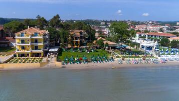 Um hotel à beira-mar com vários andares, área de praia com espreguiçadeiras e guarda-sóis, e vista para o mar.