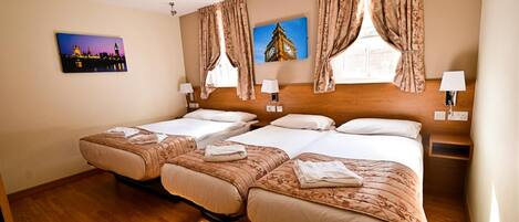 Quarto de hotel com duas camas, soalho de madeira e cortinas.