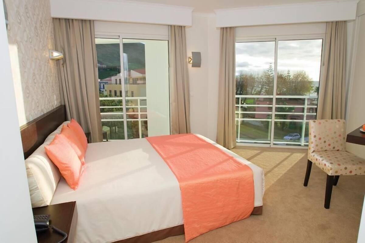 Quarto de hotel com cama, uma cadeira e vista para o exterior.