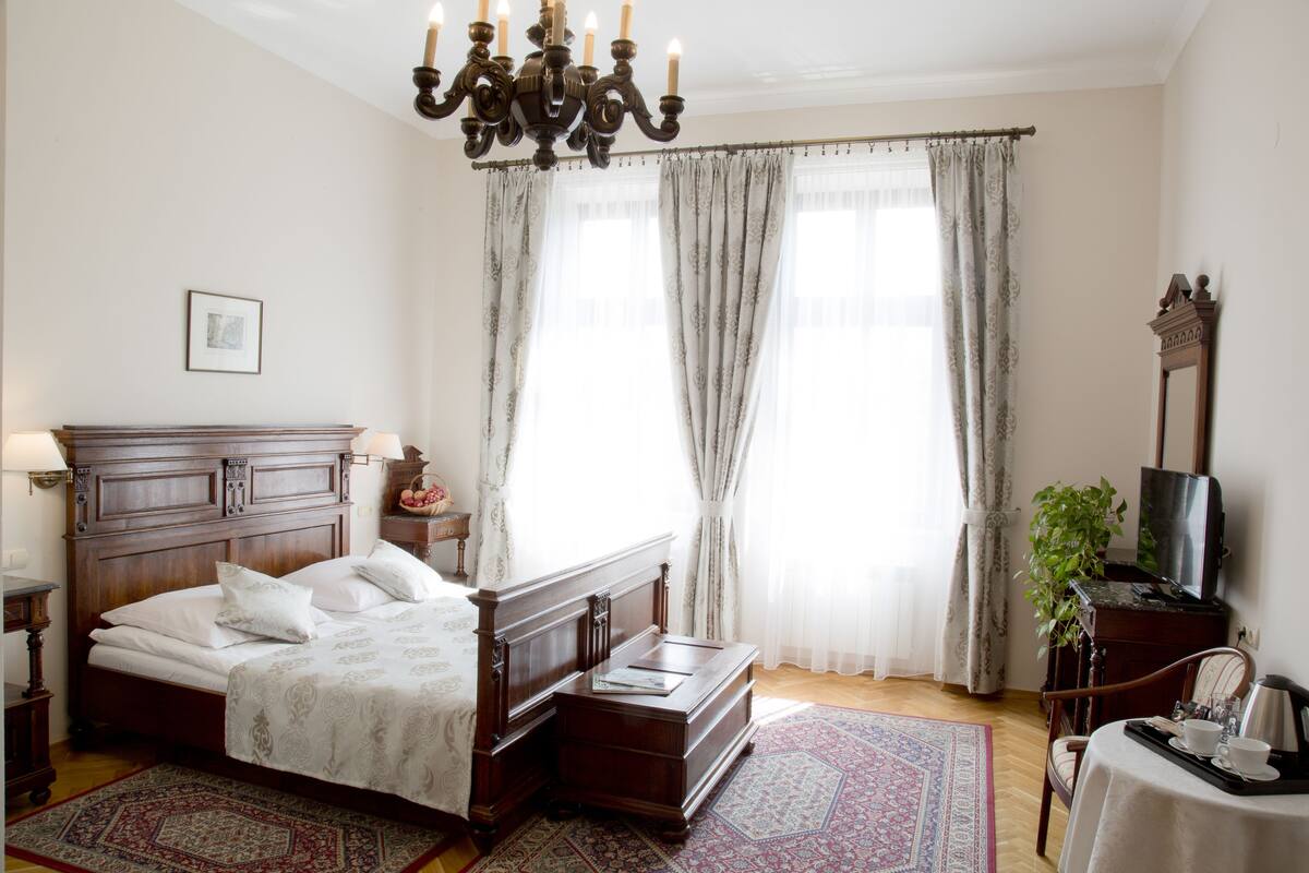 Quarto bem iluminado com uma cama grande, cômoda de madeira, televisão e escrivaninha com cadeira.