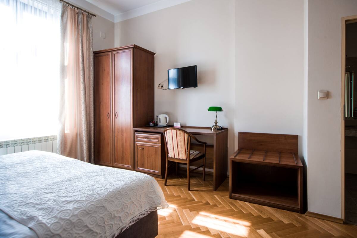 Quarto com cama, escrivaninha com cadeira, televisão e uma pequena mesa.