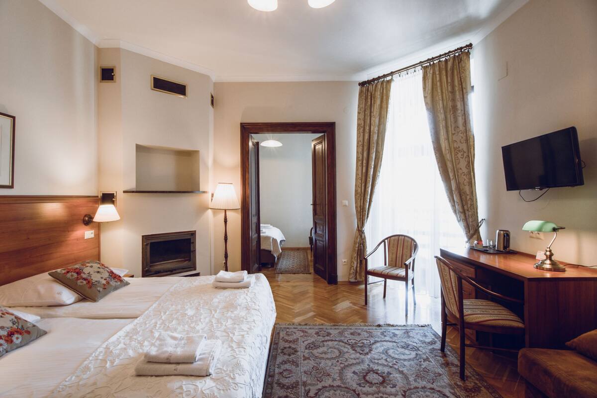 Quarto de hotel com cama, escrivaninha, cadeira, televisão e lareira.