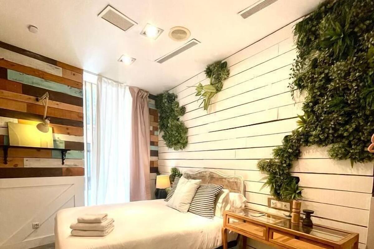 Quarto moderno com cama, mesa de cabeceira e planta fixada na parede.