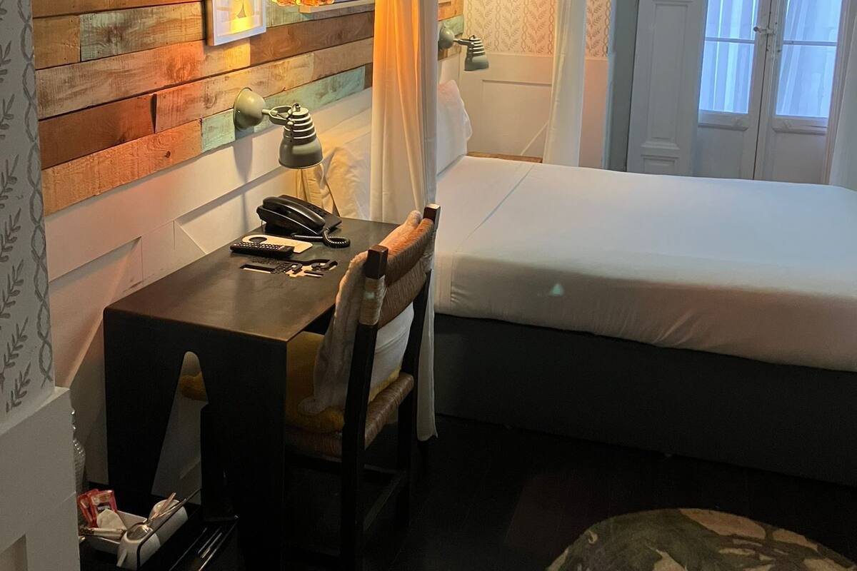 Quarto com parede de madeira, uma cama, escrivaninha com telefone e uma cadeira.