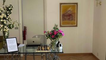 Uma área de refeições com uma mesa de vidro, cadeiras de metal, um laptop e um vaso com flores.