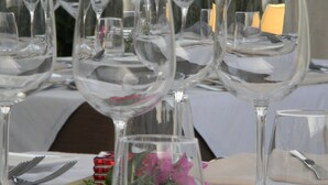 Mesa posta com vários copos de vinho, garfos e colheres, com uma vela e flores sobre a mesa.