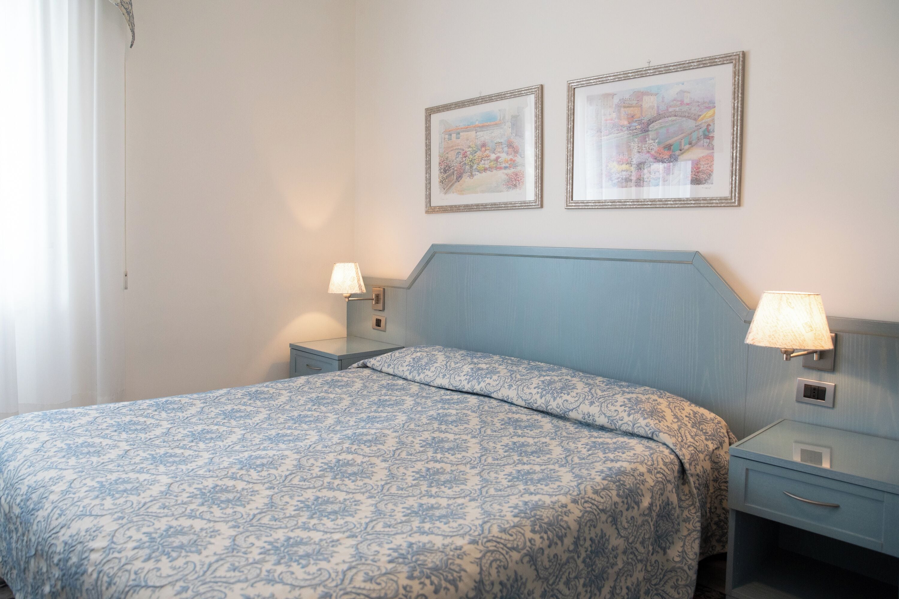 Quarto com uma cama, duas mesas de cabeceira e duas luminárias de parede.