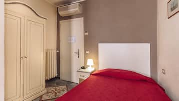 Quarto de hotel com cama, mesa de cabeceira com abajur, guarda-roupa e aparelho de ar condicionado.