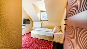 Quarto de hotel pequeno com cama, televisão e janela.