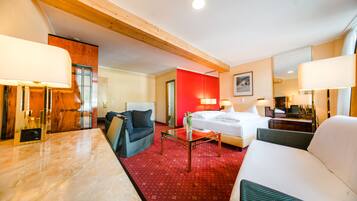 Quarto de hotel com cama, sofá, mesa de centro e escrivaninha com luminária.