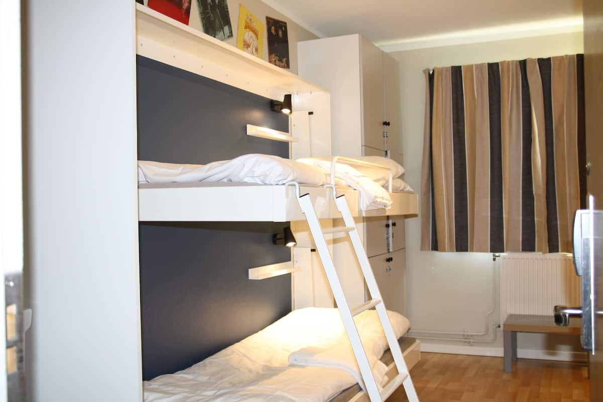 Quarto com beliche, radiador, cadeira e janela com cortinas listradas.