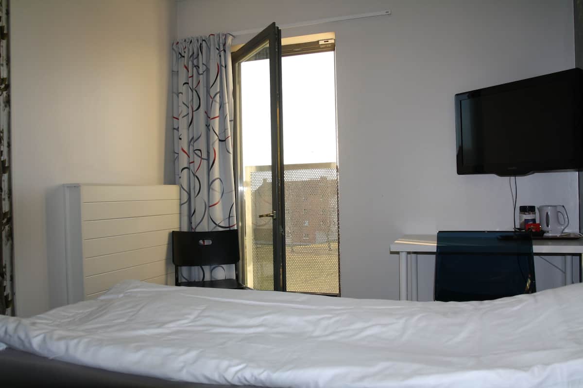 Quarto de hotel com uma cama, uma mesa de trabalho com uma televisão e vista através de uma porta.