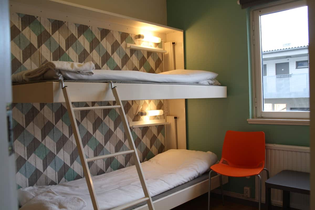 Uma cama beliche com escada, uma cadeira e uma janela com vista para edifícios.
