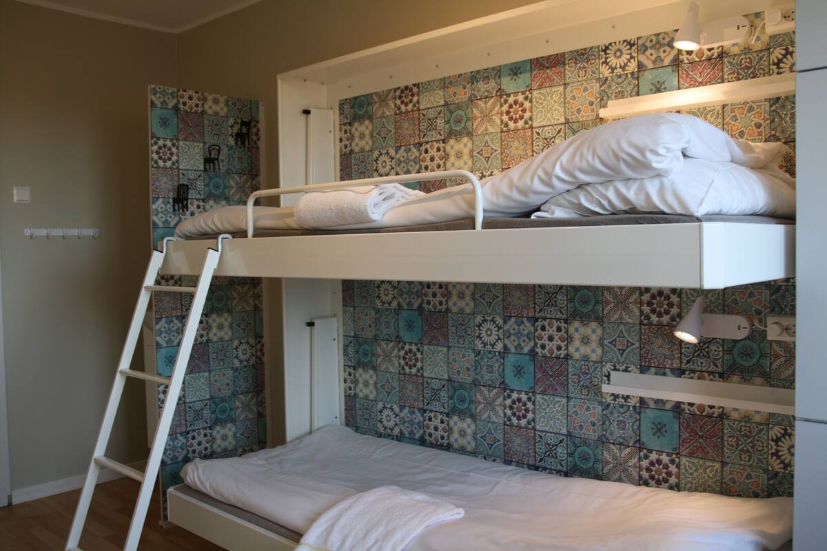 Uma cama beliche com escada, uma cama de solteiro embaixo e uma parede colorida com padrão.