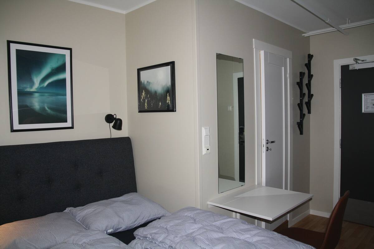 Quarto com cama, escrivaninha e espelho.