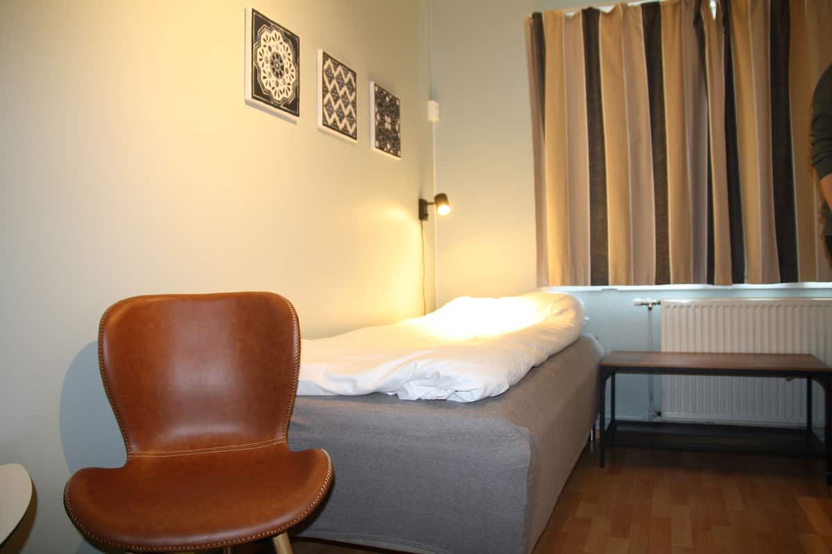 Um quarto com uma cama, uma cadeira, uma mesa de cabeceira e uma janela com cortinas.