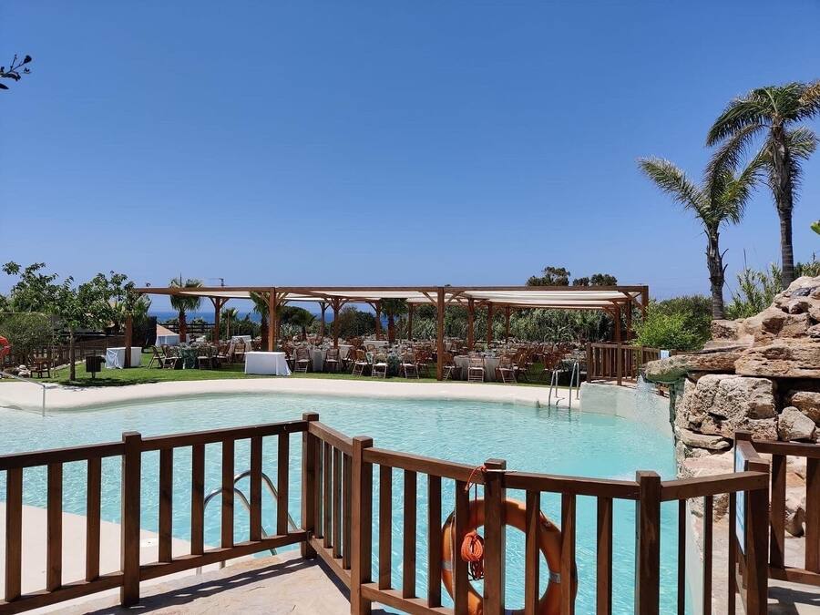Uma área de piscina com deck de madeira, espreguiçadeiras e um espaço de refeições coberto, com mesas e cadeiras.