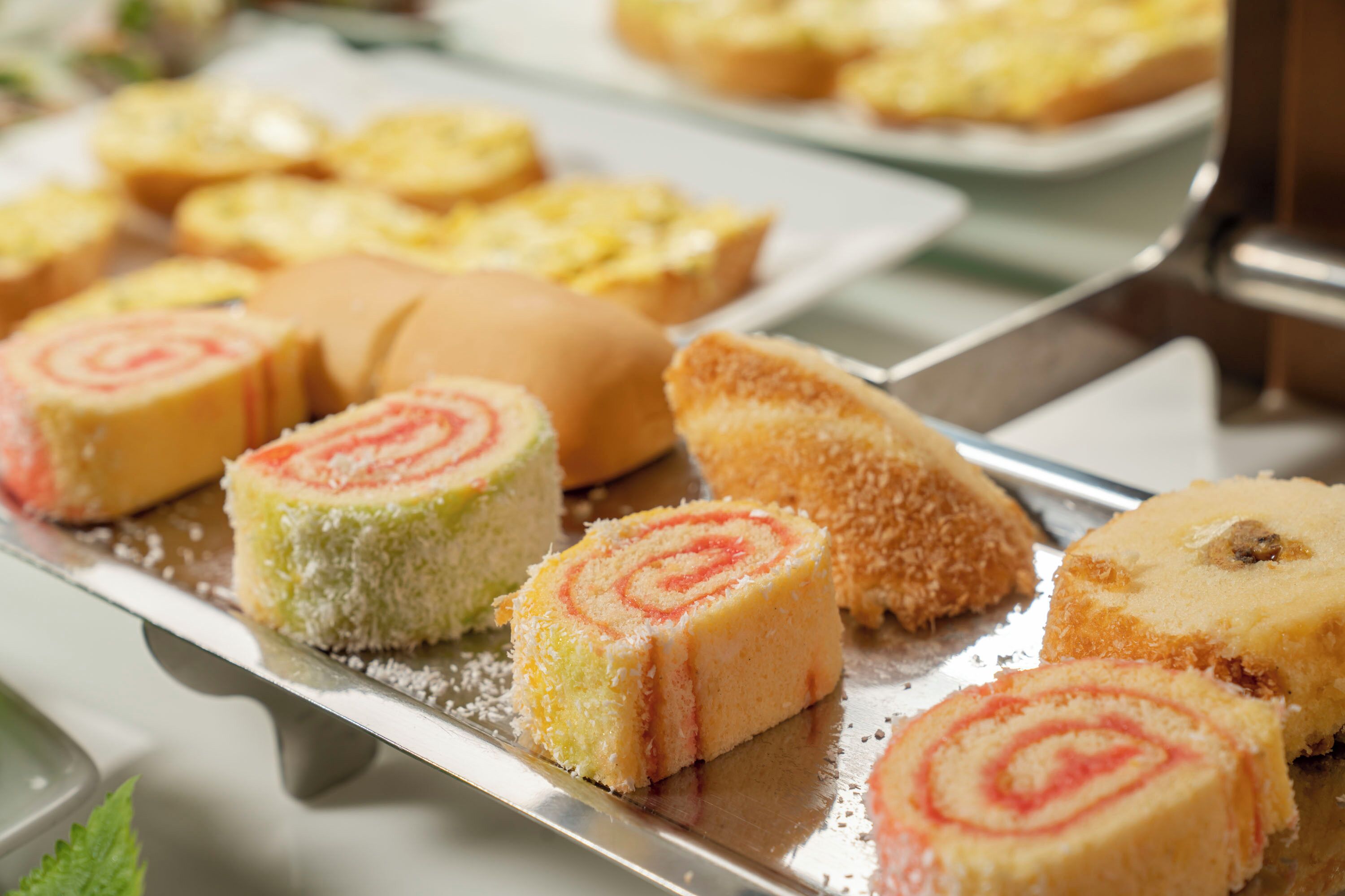 Uma mesa de buffet com diversos alimentos, incluindo um pão com padrão espiral vermelho e branco, uma fatia de pão e outras opções de pastelaria.