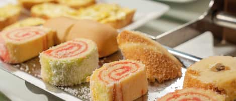 Uma mesa de buffet com diversos alimentos, incluindo um pão com padrão espiral vermelho e branco, uma fatia de pão e outras opções de pastelaria.
