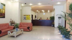 Uma área de recepção com dois sofás laranja, uma mesa de centro de vidro e um balcão de atendimento com dois funcionários.