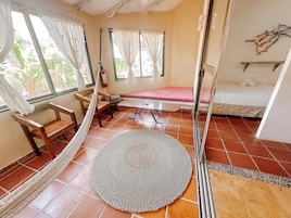 Um quarto com rede, um tapete redondo de palha, uma cama e um banco.