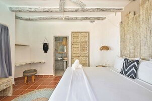 Quarto com cama, porta de madeira, um pequeno banquinho e prateleira na parede.