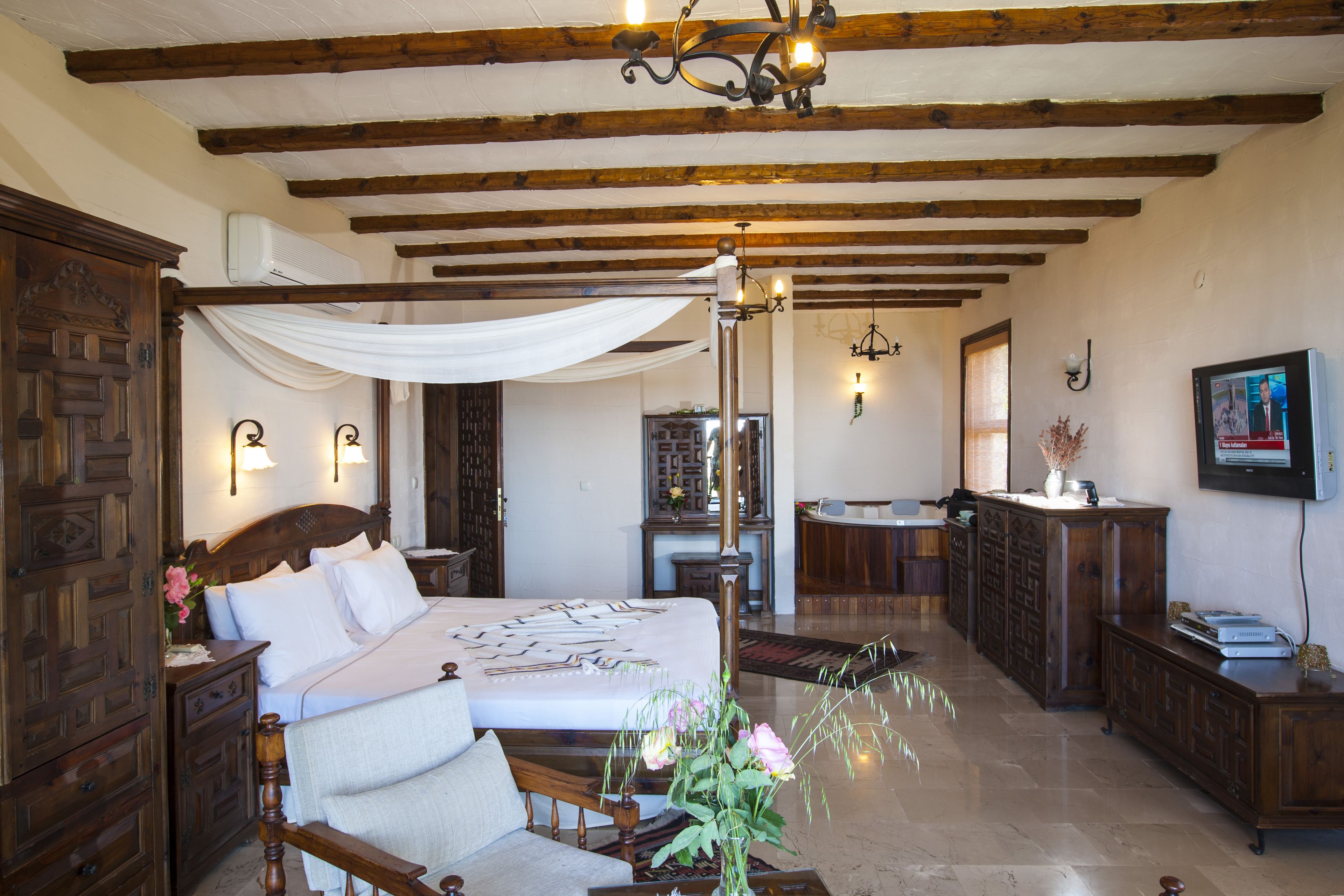 Quarto de hotel com uma cama grande, móveis de madeira, um candelabro e uma TV de tela plana.