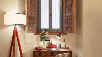 Quarto de canto com escrivaninha, cadeira, abajur e janela com persianas abertas.