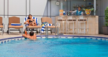 Uma área de piscina com espreguiçadeiras, um bar e um relógio na parede.