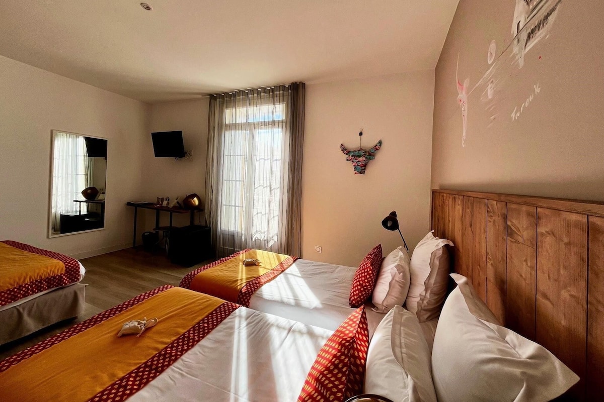 Quarto de hotel com duas camas, uma escrivaninha, uma cadeira, televisão e janela com cortinas.