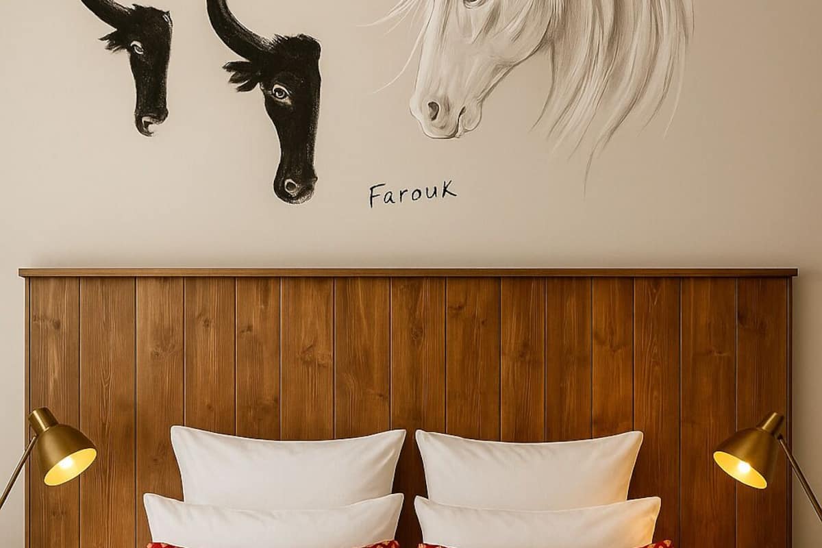 Quarto com cabeceira de madeira, duas almofadas brancas com capas vermelhas estampadas, e dois chifres de vaca pretos e uma cabeça de cavalo branca na parede.