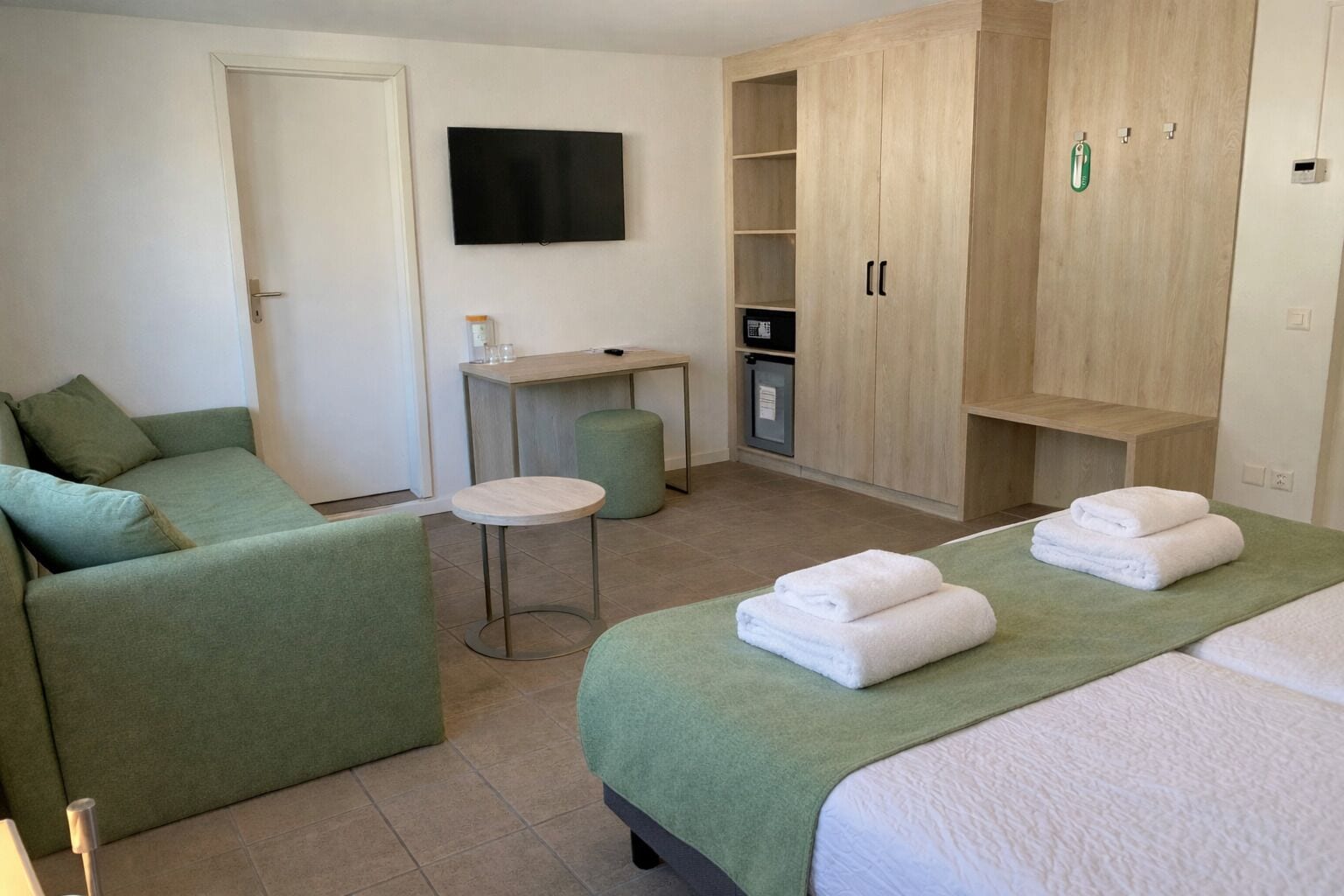 Quarto de hotel com cama, sofá, escrivaninha e televisão.