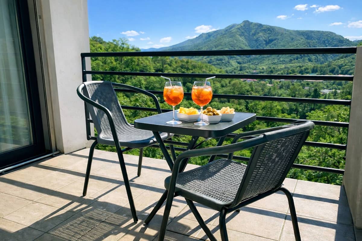 Uma varanda com duas cadeiras, uma mesa, dois copos de bebida de laranja e uma tigela de petiscos.