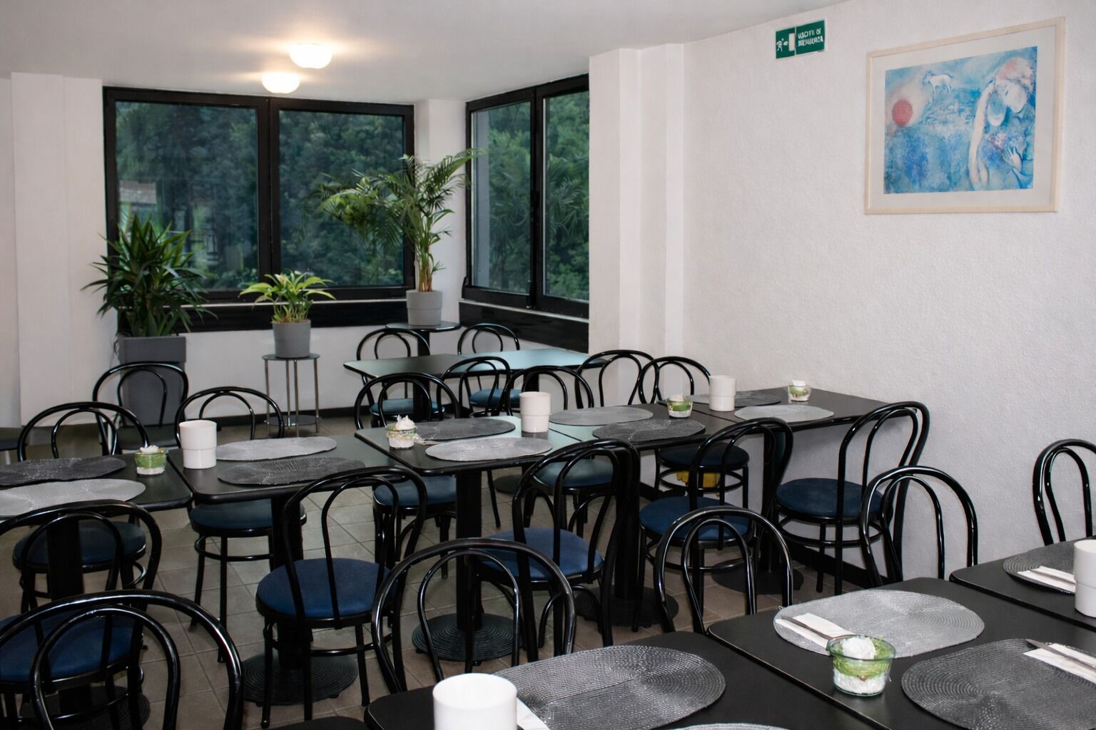 Uma sala de jantar com várias mesas e cadeiras, plantas em vasos e obras de arte nas paredes.