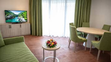 Uma sala de estar moderna com um sofá verde, uma mesa de jantar com cadeiras, uma televisão em um móvel e uma janela com cortinas.